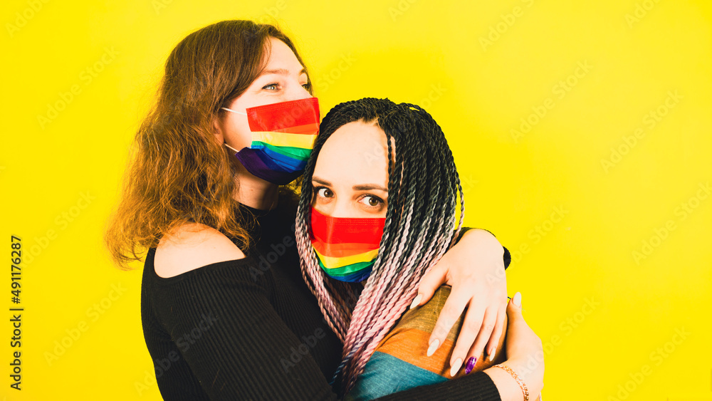 Lesbian couple in rainbow masks embracing in studio. Side view of LGBT ...