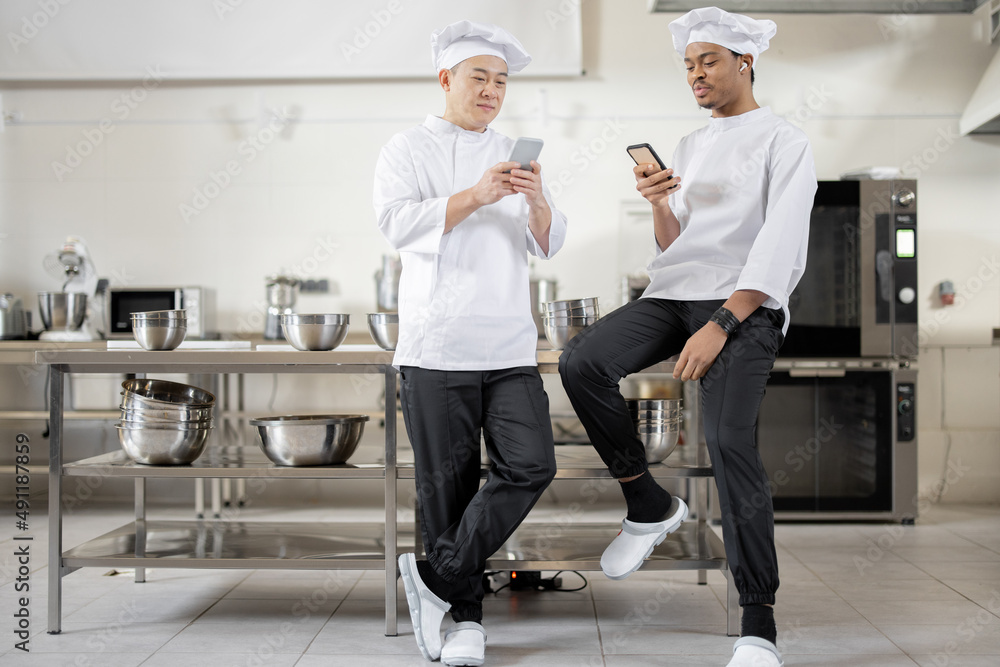 Two multiracial chef cooks standing with smart phones during a break at ...
