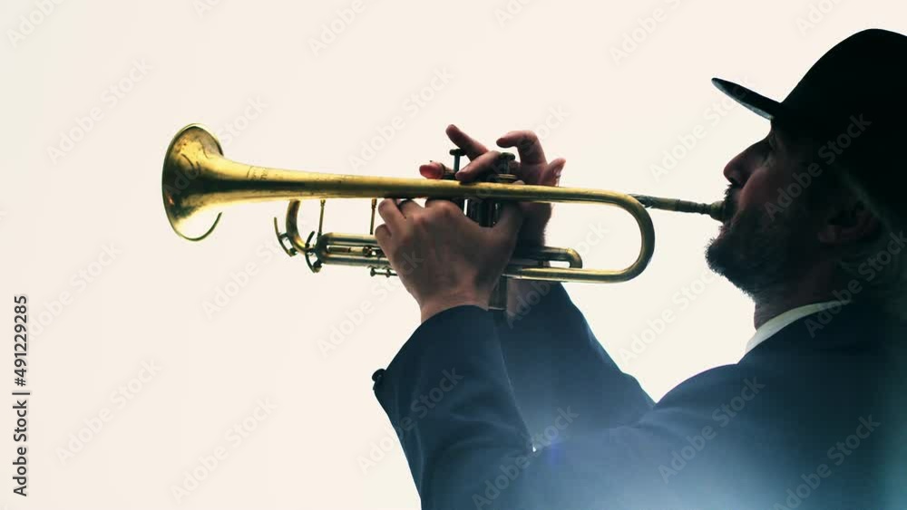 Musician in hat raises musical trumpet and begins to blow, pressing ...