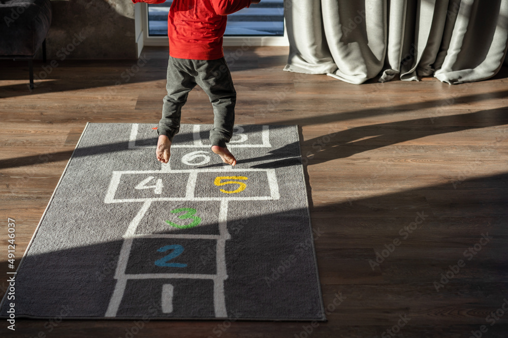 Child, toddler, little boy playing hopscotch, jumping on carpet ...