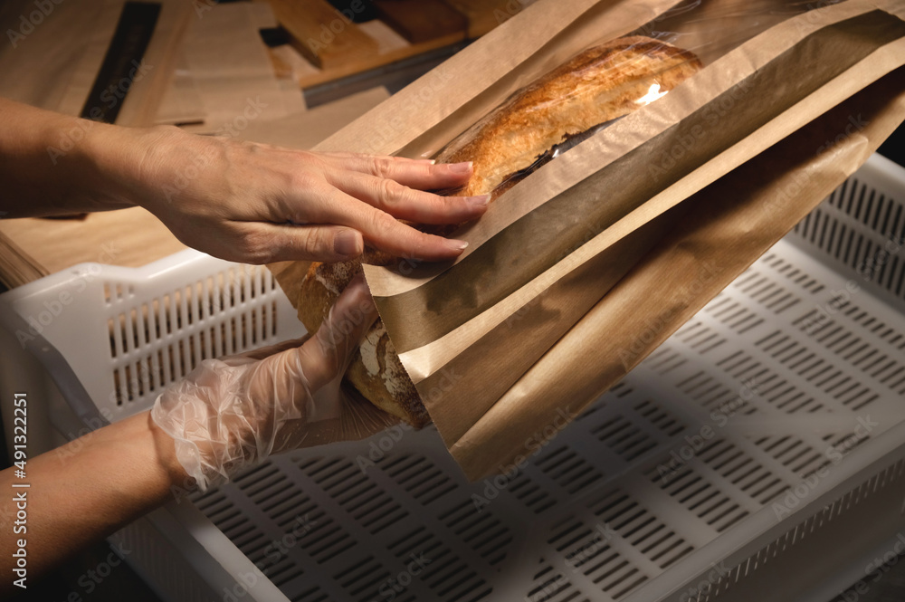 Close-up of female hands packing fresh artisanal bread in a paper bag ...