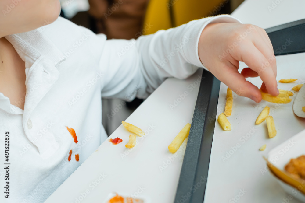 Children's hand holding french fries potato chips at the table in a ...