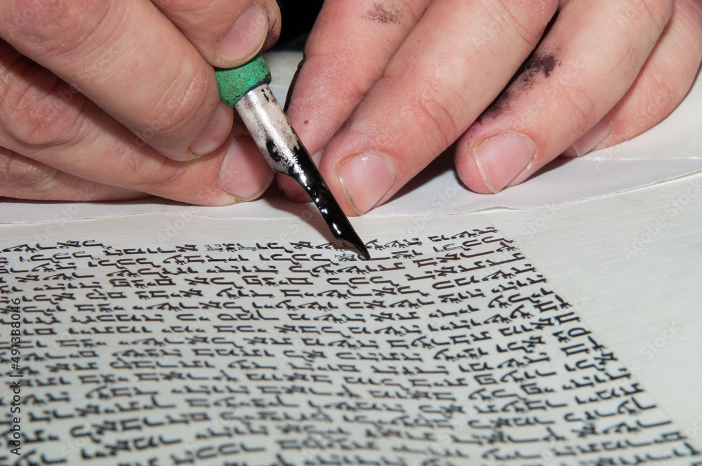 Closeup view of the hands of a Jewish scribe writing the Hebrew text of ...