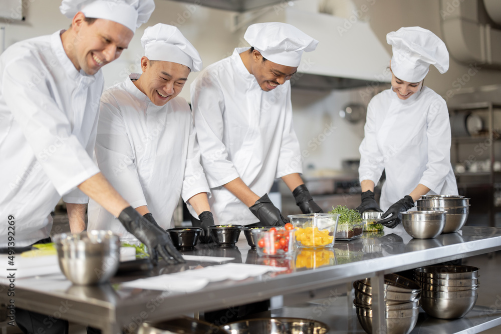 Multiracial team of cooks mixing ingredients for take away food in ...