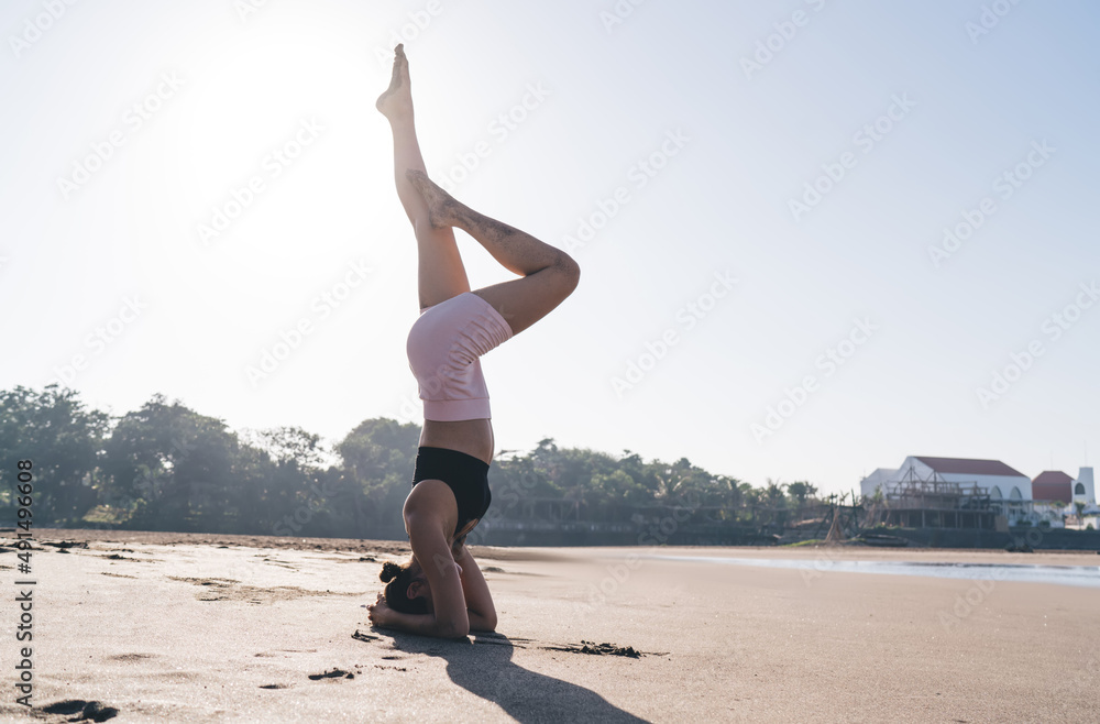 Strong female with athletic body standing on hands and head in asana ...
