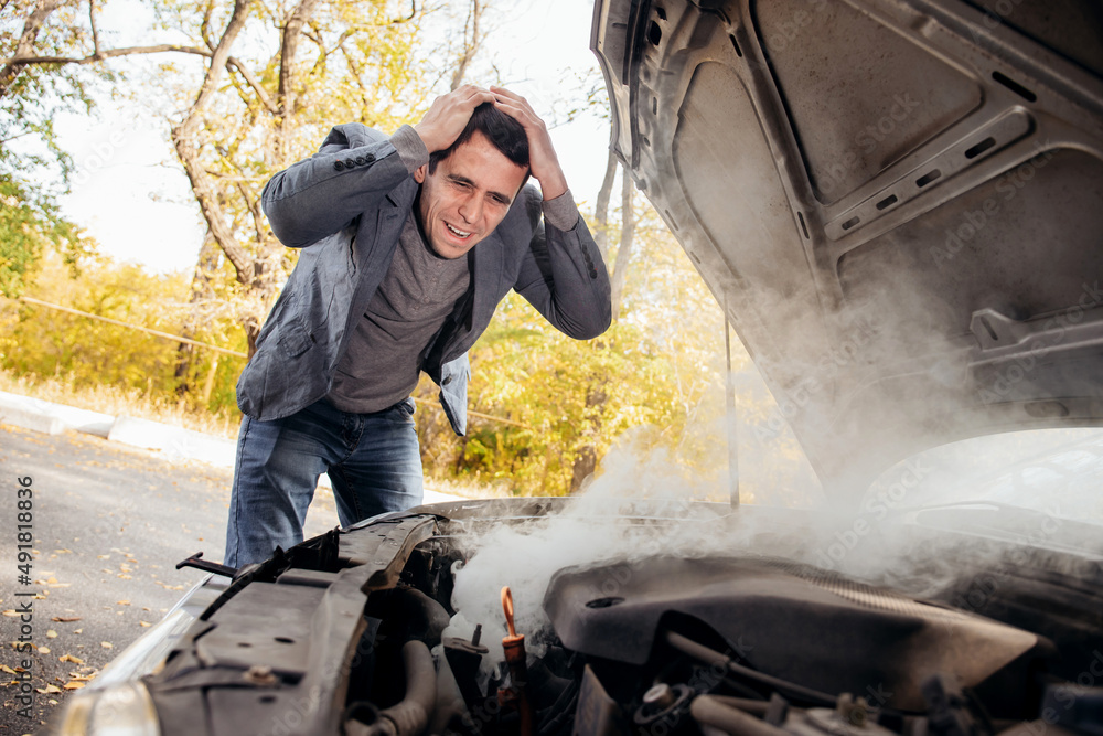 A man looks under the open hood of a car. The car broke down on the ...