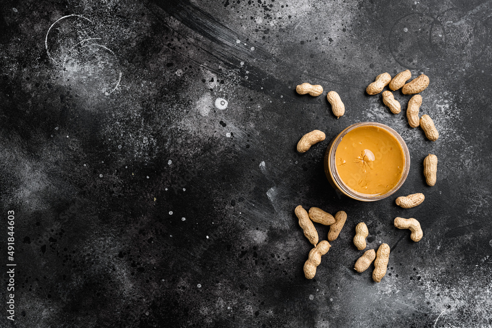 Peanut paste in an open jar and peanuts, on black dark stone table ...