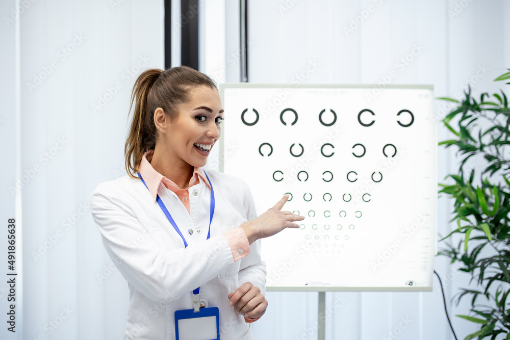 Professional female optician pointing at eye chart, timely diagnosis of ...