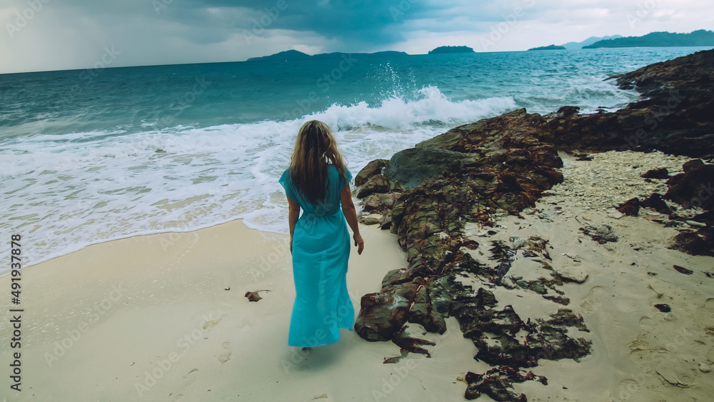 Alone attractive woman walk in beach, near a rock reef hill in stormy ...