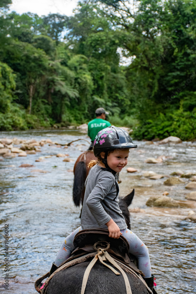Child horse riding in the amazon jungle. Guide is leading the crossing ...