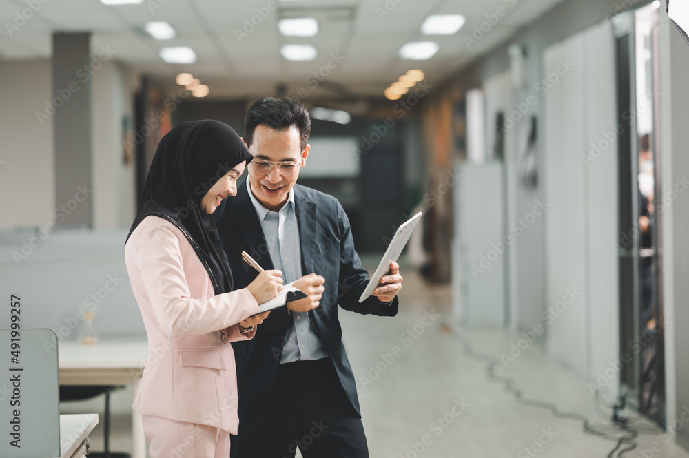 Middle-aged businessman and female secretary wearing hijab stand ...