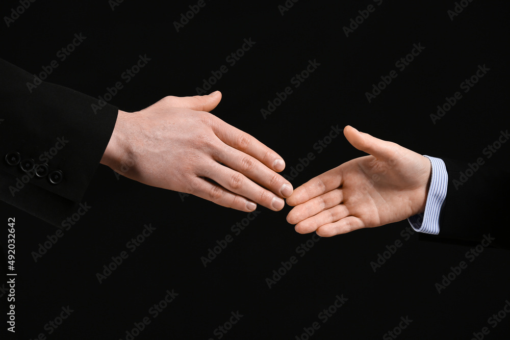 Business workers reaching out to handshake on black background, closeup ...