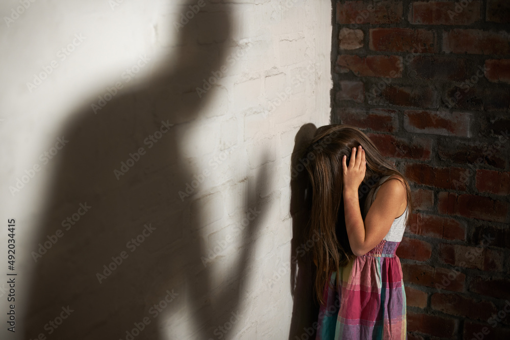 Defenceless victim. Abused little girl huddled over while the shadow of ...