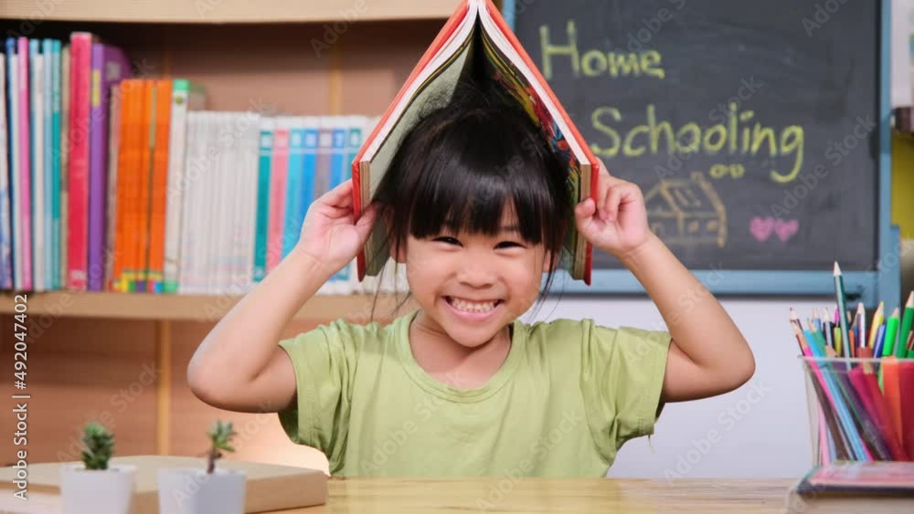 Cute little girl holding a book over her head like a roof, smiling and ...