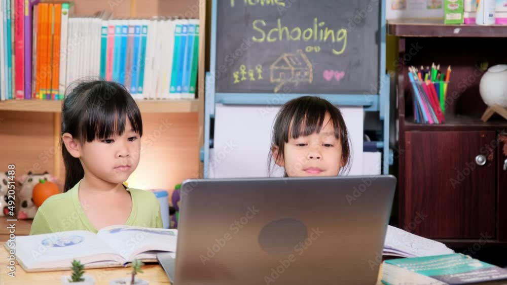 Two Asian female students study online video call Zoom with laptop at home. Two little girls ...