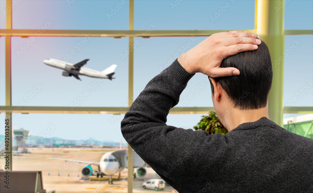Rear view of a sad man looking at a plane taking off and missing his ...