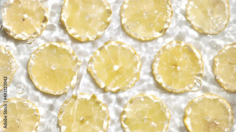 Pouring water splashing and making ripples over lemon slices arranged ...