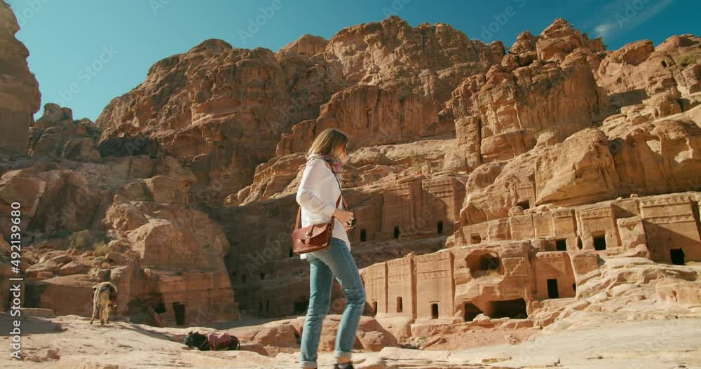 Female tourist visits Petra taking photo of ancient caves carved out of ...