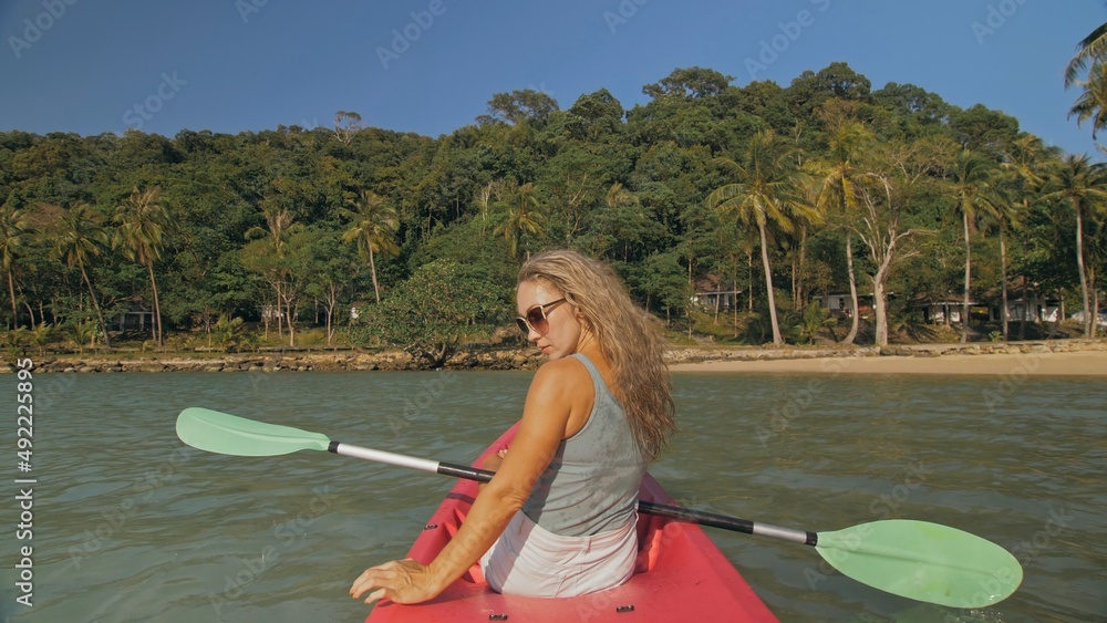 Long haired blonde woman with sunglasses rows bright pink canoe along ...