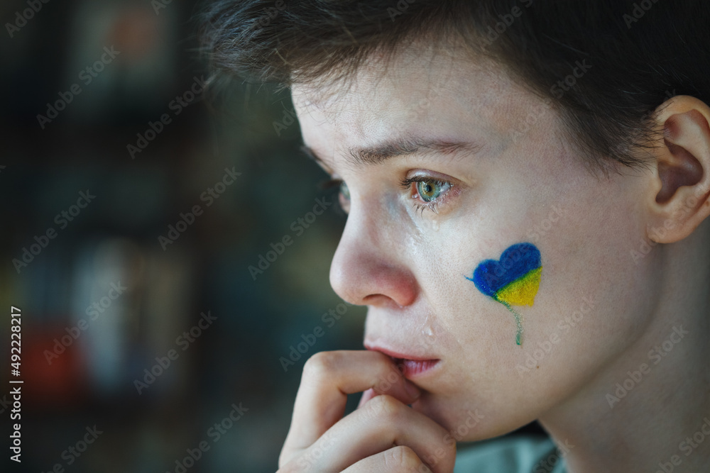 Young sad woman with Ukrainian flag symbol on her face crying, stop the ...