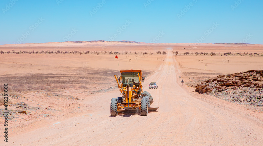 Perspective road background of Yellow grader smooths dirt road in namib ...