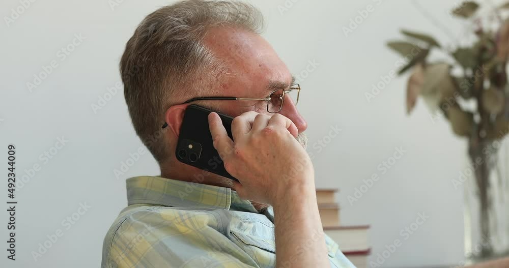 Close up side face view of 60s man sit indoors holds cellphone lead ...