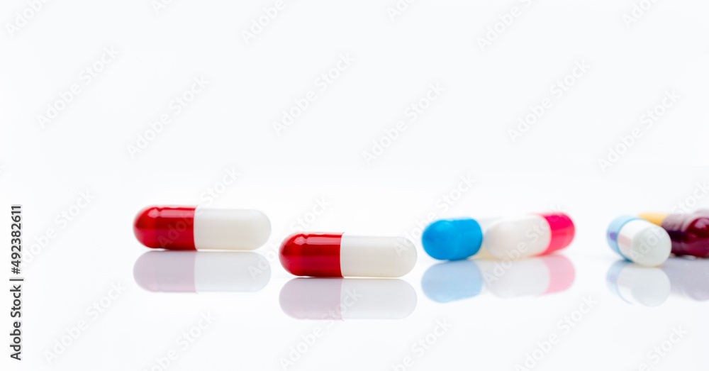 Red-white antibiotic capsule pill on blur multi-colored capsules ...