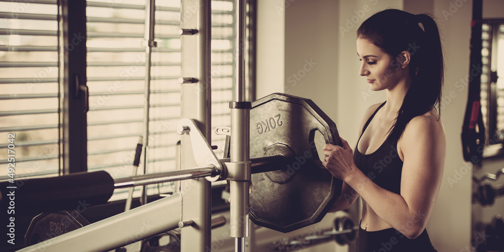Woman adding weight on a bar as she workout in fitness gym banner size ...