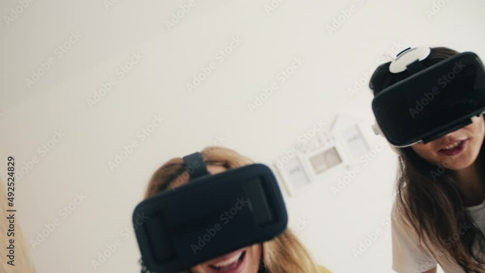 Exited girls in VR helmets at home. Two women in virtual reality ...