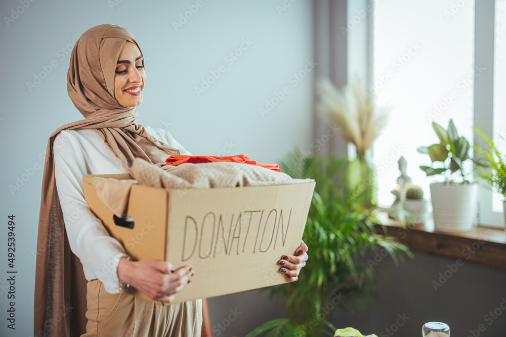 Poster Young cheerful Muslim woman standing and holding a cardboard ...
