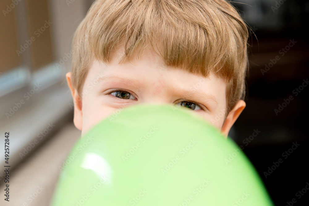 3 year old boy inflating green balloon with a mouth. Swollen cheeks and ...