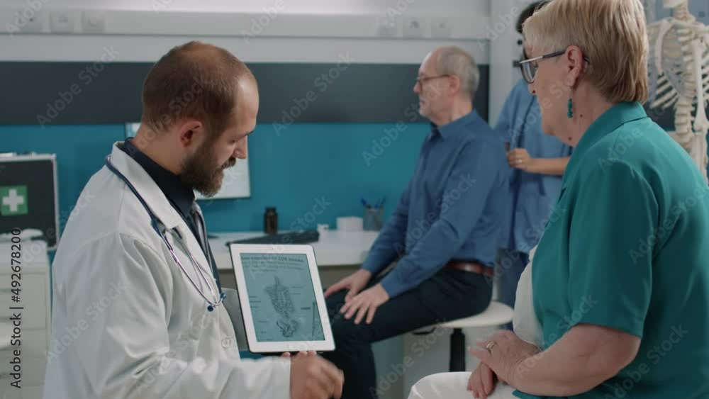 Male osteopath showing human skeleton illustration on tablet ...