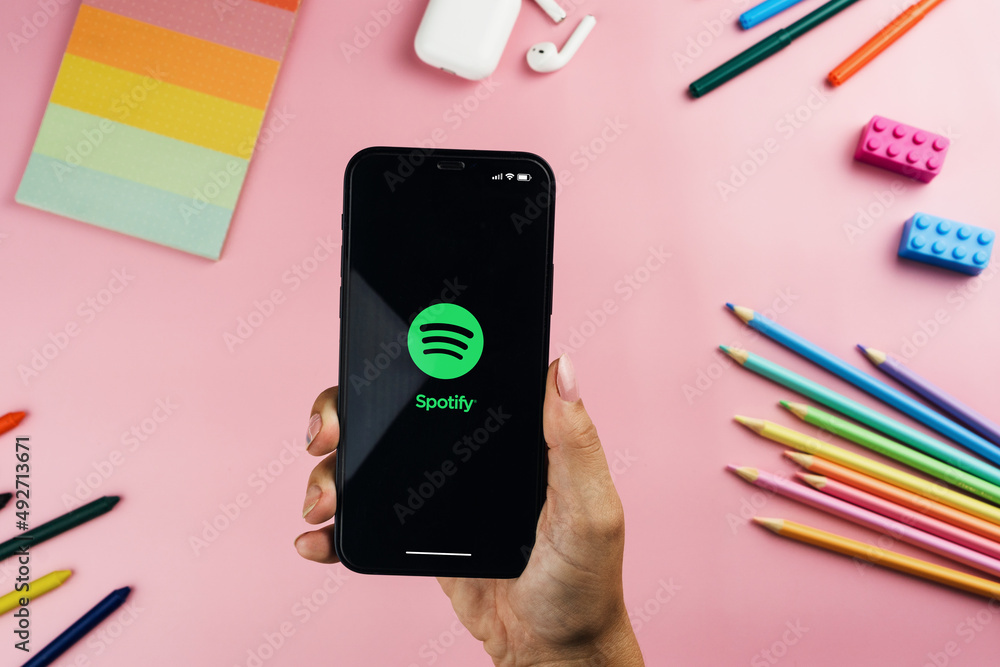 Girl holding a smartphone with Spotify Music app on the screen. Pink ...