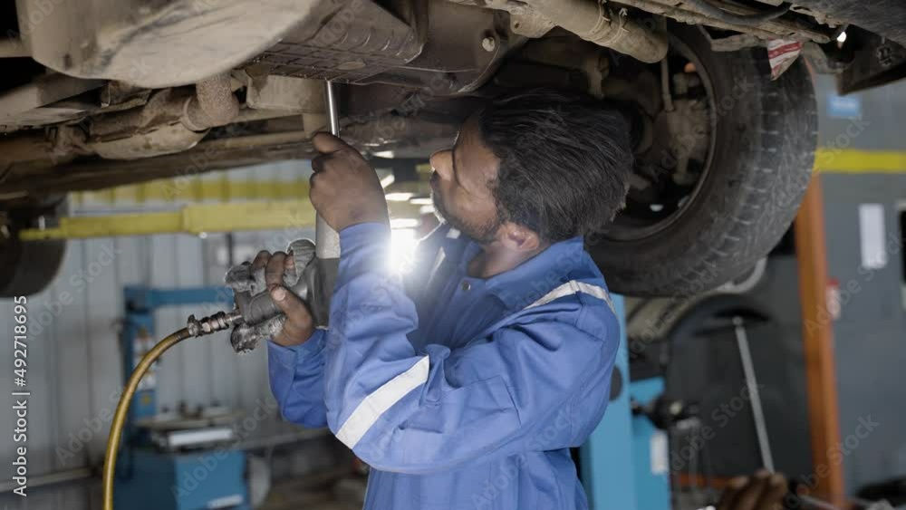 Car mechanic in uniform busy working using tools in under lifted ...