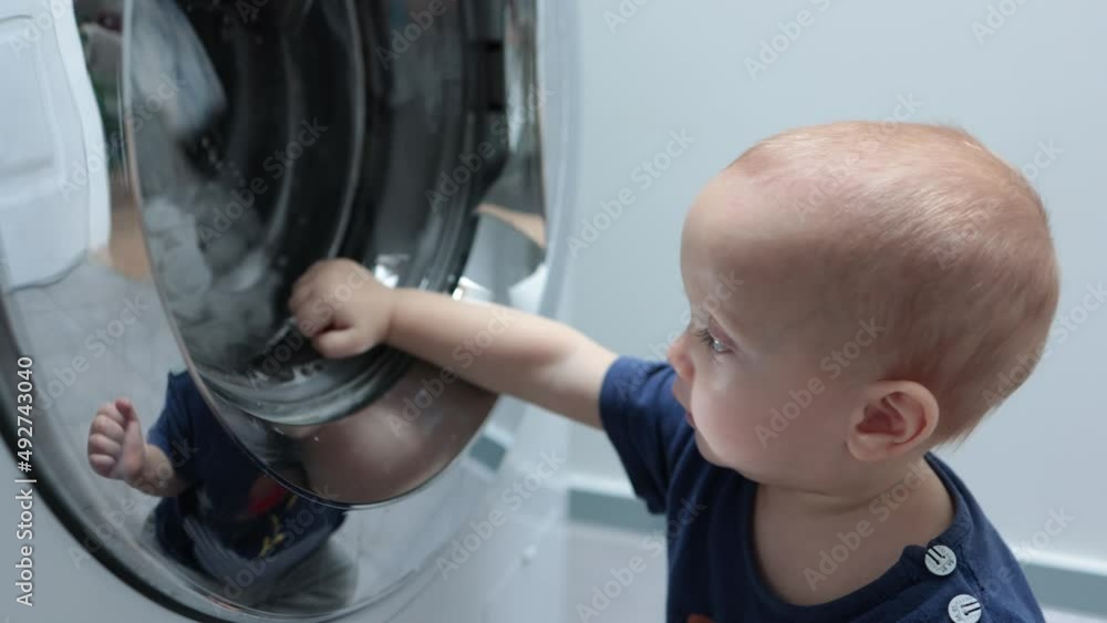 little baby toddler kid looking at working washing machine laundry ...
