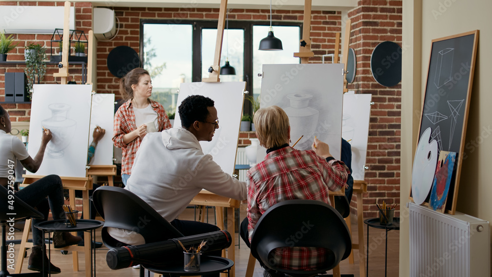 Elder woman and young man learning to draw sketch on canvas, talking in ...