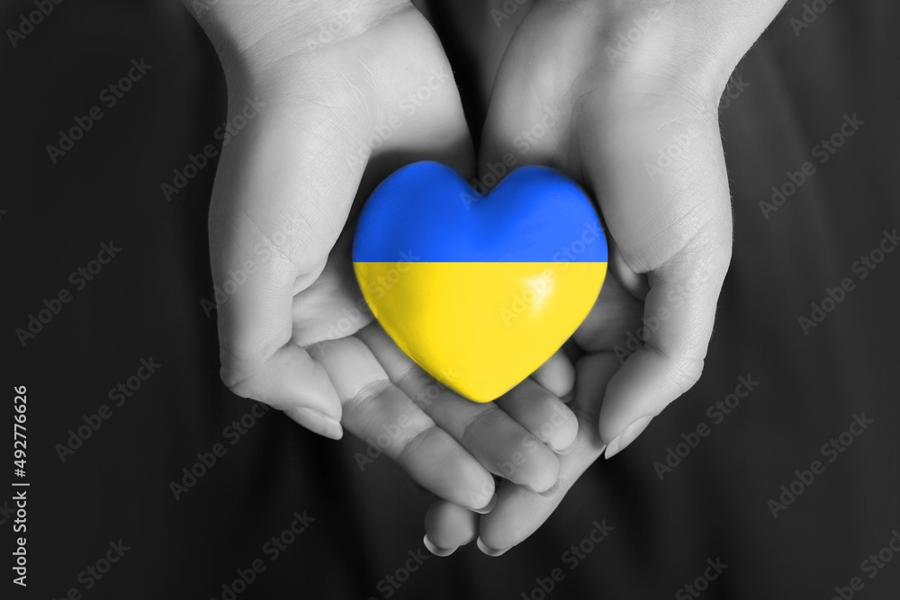 Women's hands hold a heart in the colors of the Ukrainian flag. pray ...