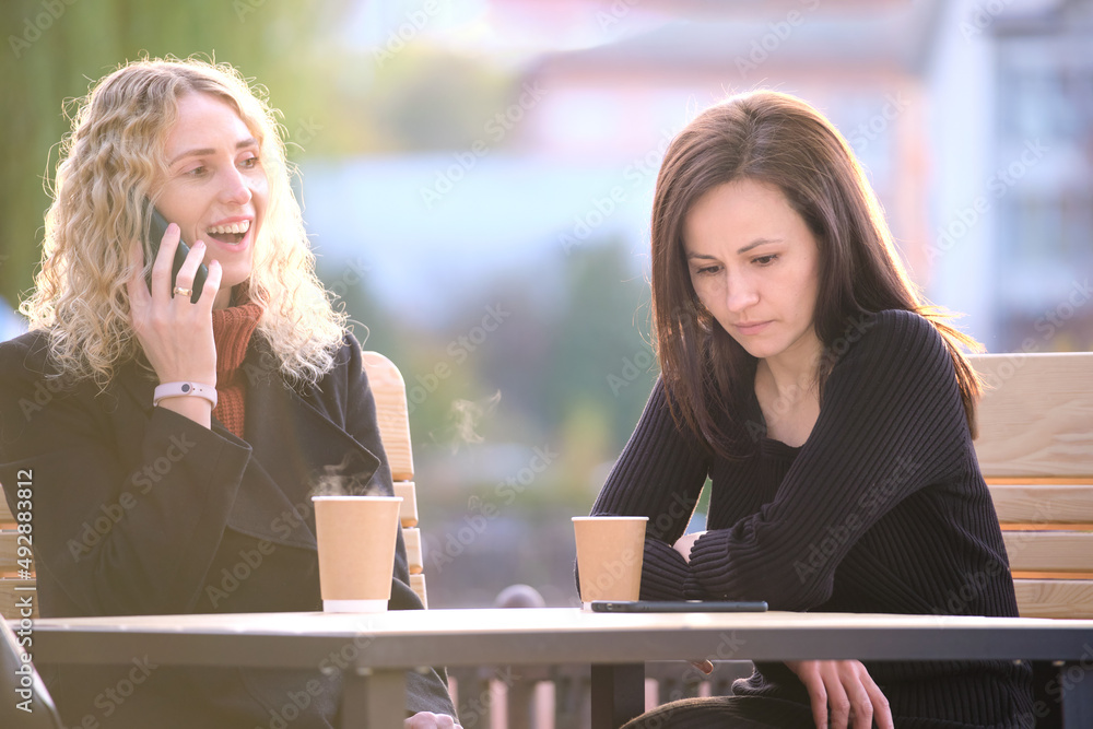 Sad woman being ignored by her friend sitting at street cafe outdoors ...