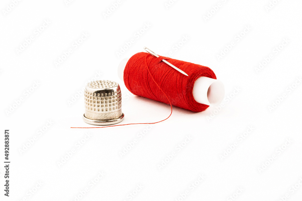 Spool of red thread with a needle and a thimble on a white isolated ...