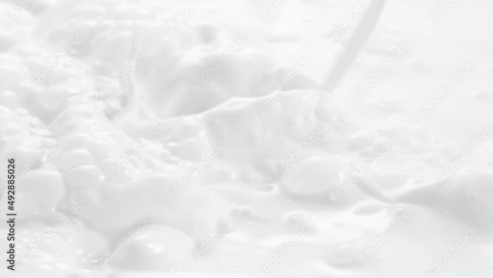 Closup of fresh milk flow pouring with splashes, ripples and bubbles ...
