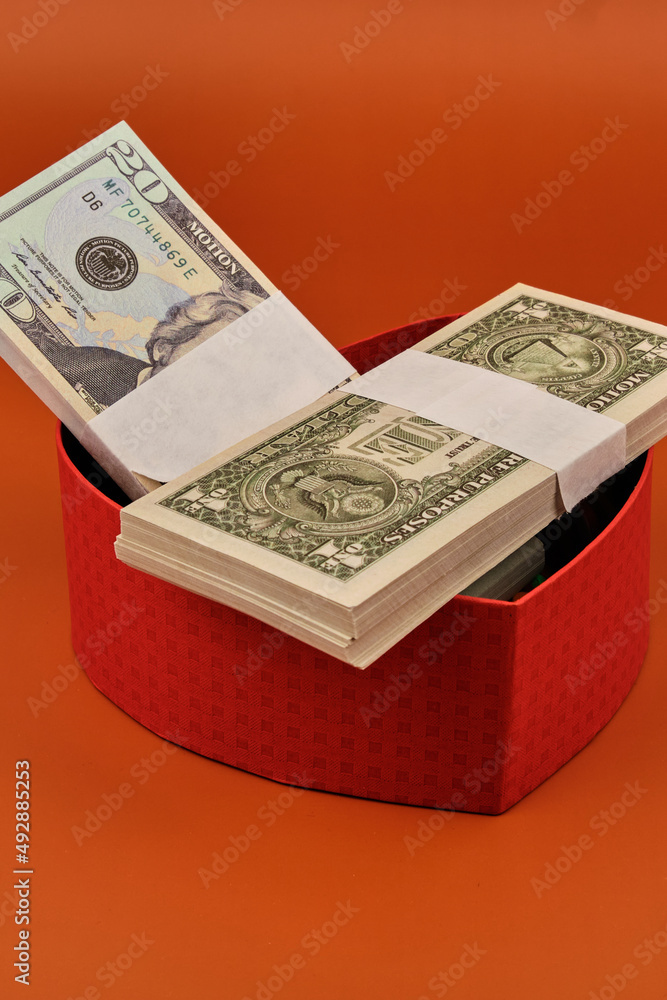Gift in the shape of a heart full of dollars with an orange background ...
