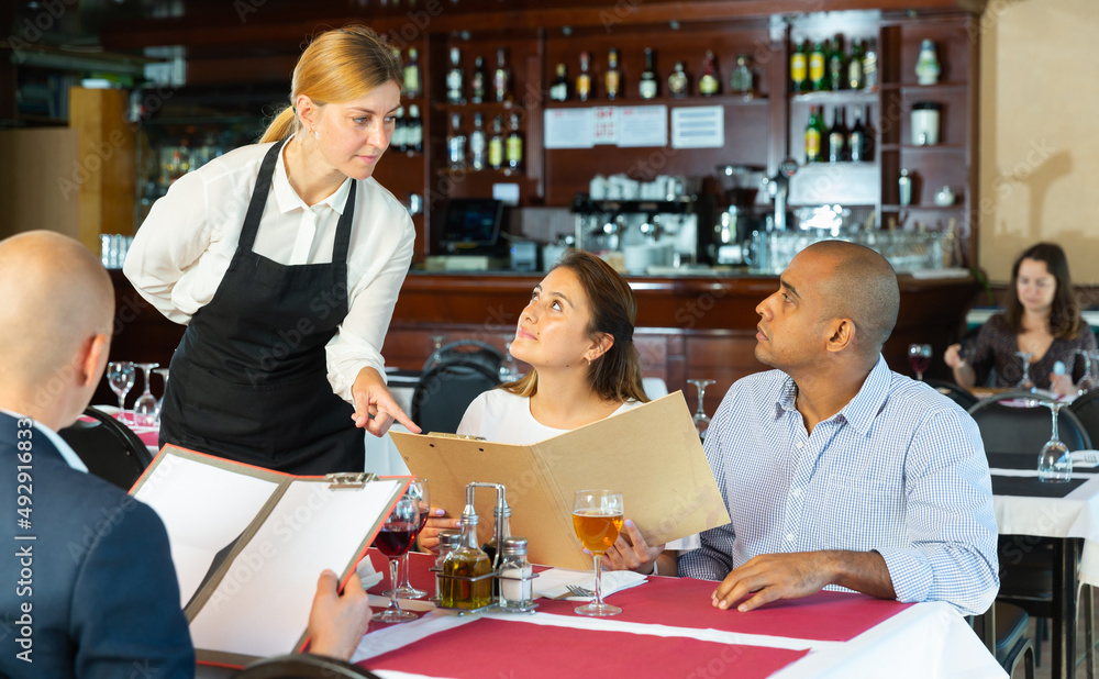 Restaurant guests will choose dish from the menu. Polite waitress helps ...