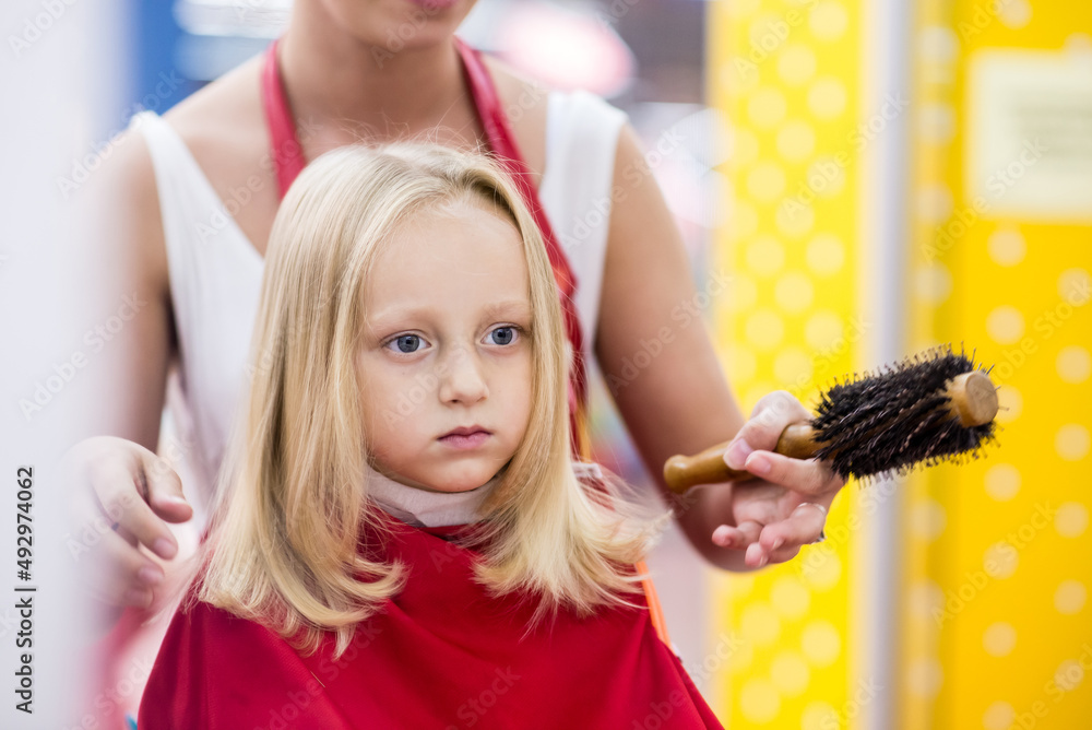Child gets her haircut from Hairdresser in beauty salon. Little girl ...