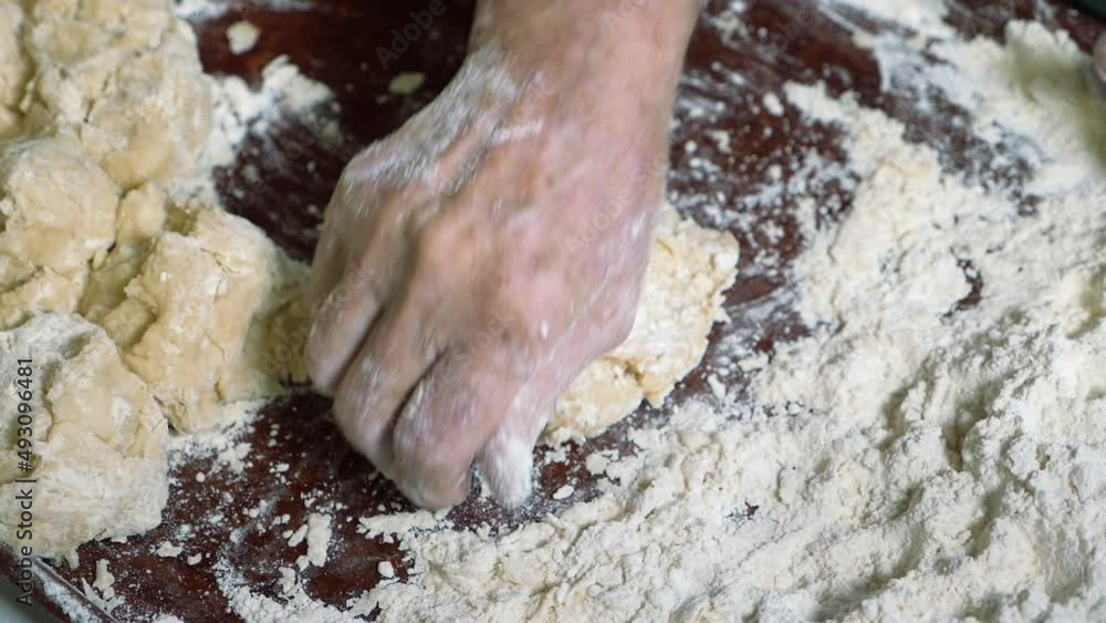 Wrinkled hands of an elderly man knead the dough and make balls of ...