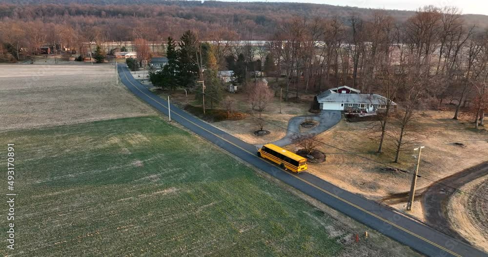School bus drives on road through rural American countryside. Homes at ...