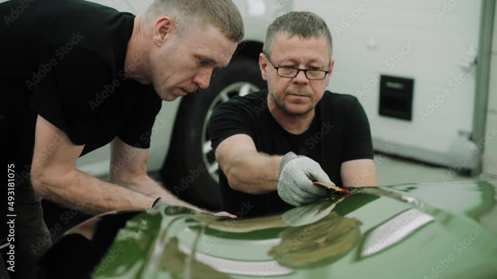 Two men are focused on the process of vinyl wrapping a car using ...
