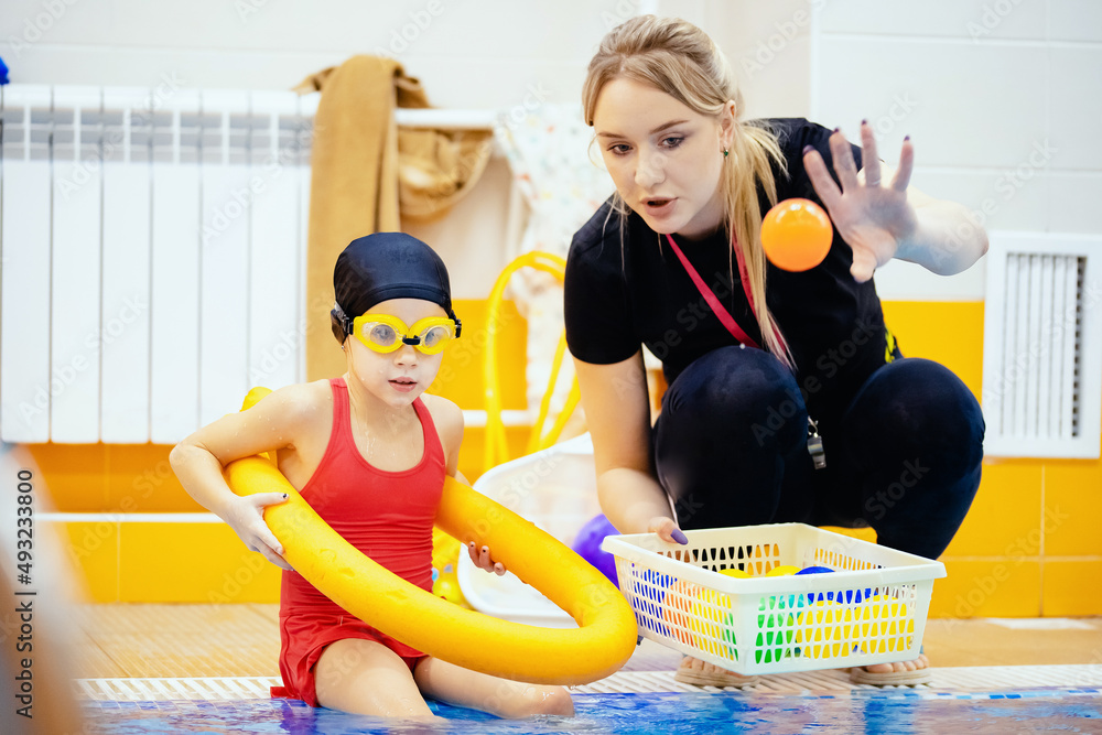 Child girl is practicing swimming in pink bathing suit in pool, coach ...