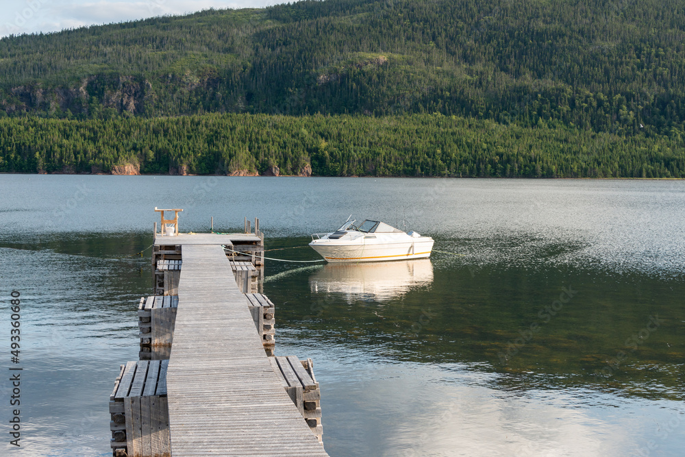 A long wooden boat wharf with a white boat moored. The plank pier juts ...