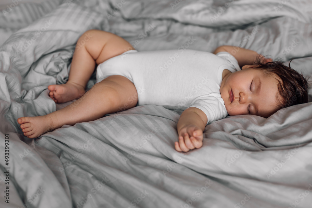 Portrait of baby in white bodysuit lying on blanket on bed. Sleeping ...