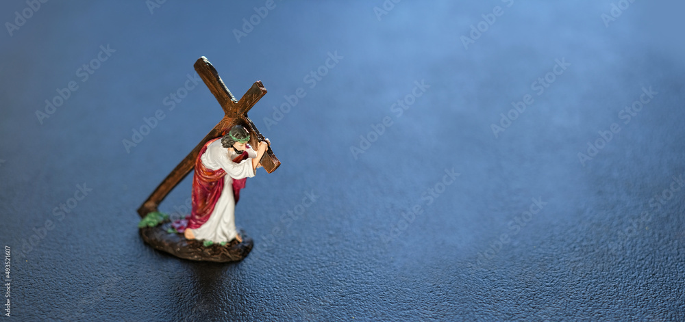Statue of Jesus Christ carrying his cross on Calvary on dark abstract ...